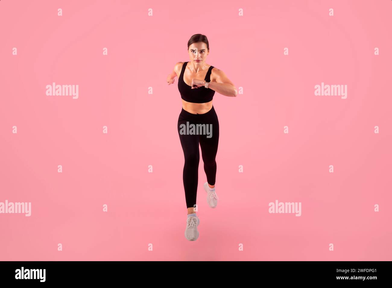 Determined female athlete running towards camera, training on pink ...