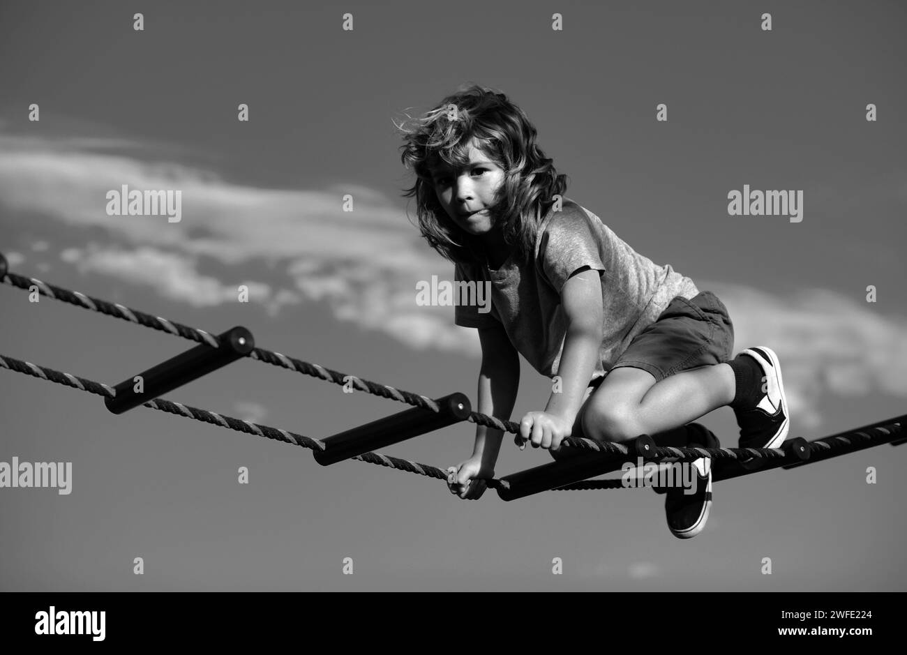Kid climbing the net. Cute boy climbs up the ladder on the playground ...