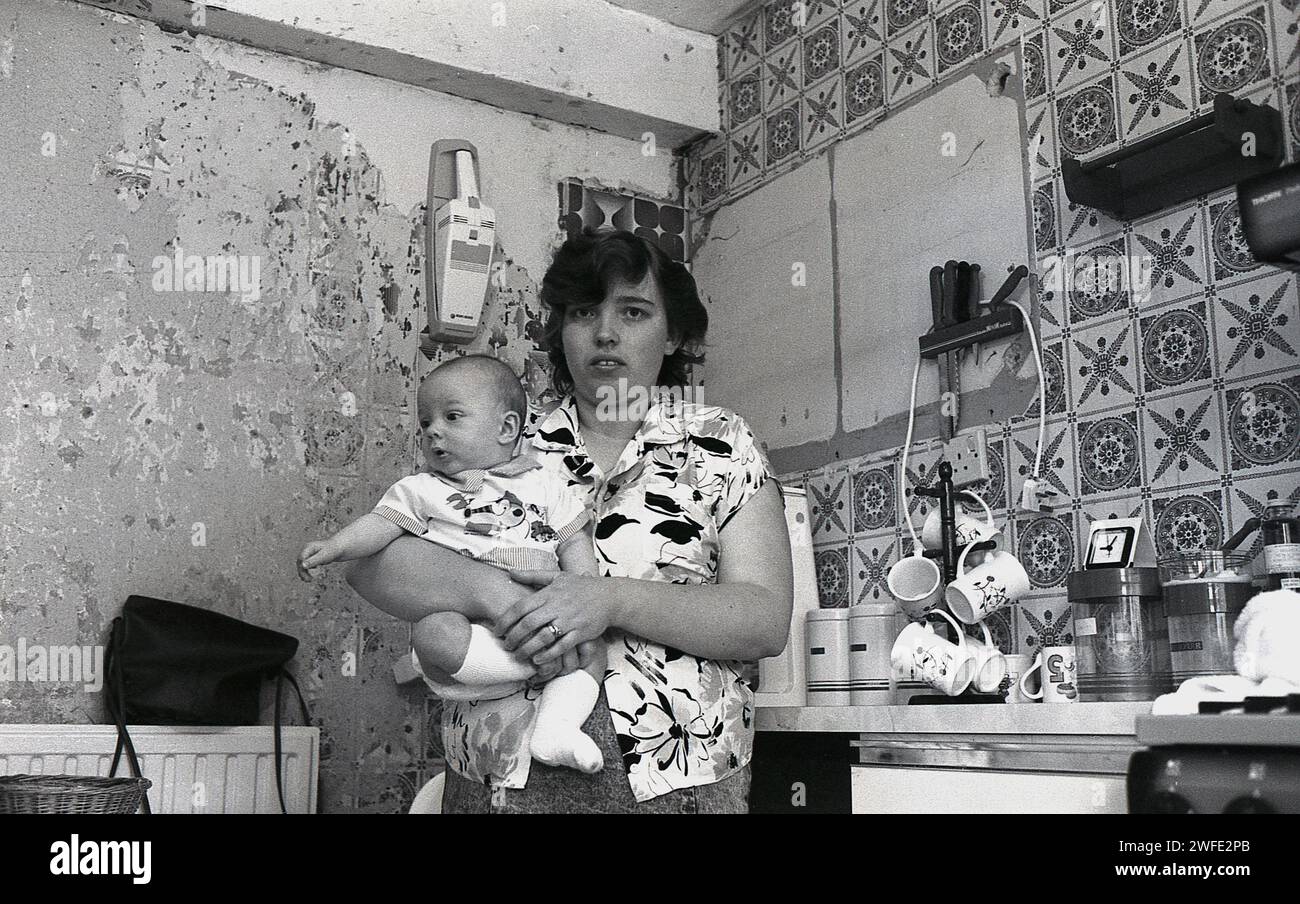 1980s, historical, a mother, middle twenties in age, holding her infant ...
