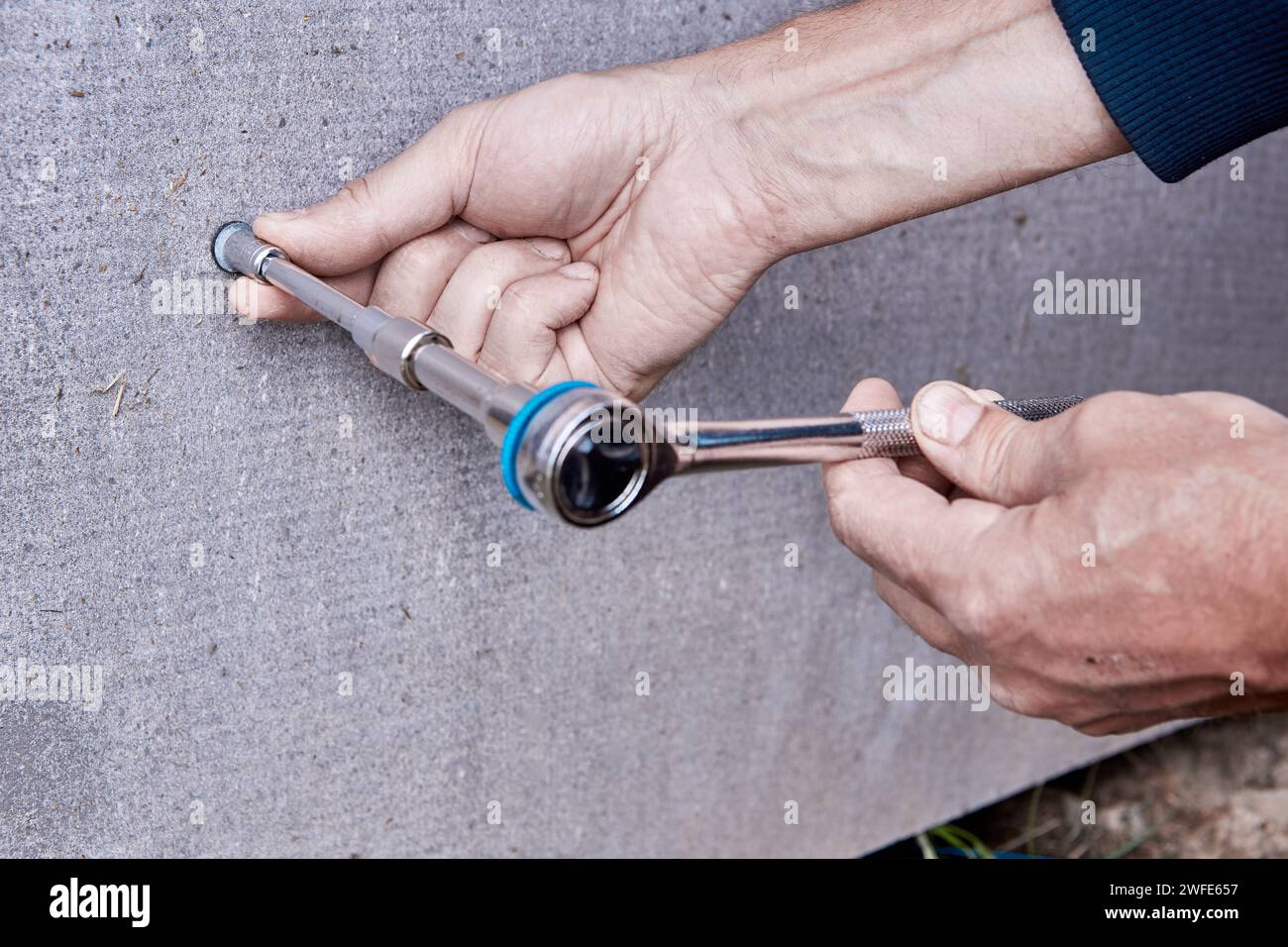 Finishing plinth on stilts with flat slate, worker uses socket wrench ...