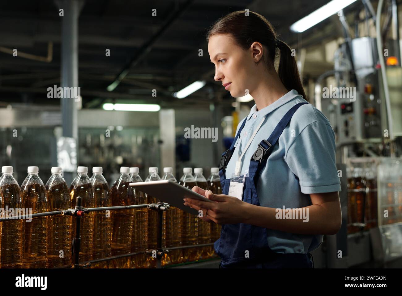 Young quality inspector with tablet standing in front of assembly line ...
