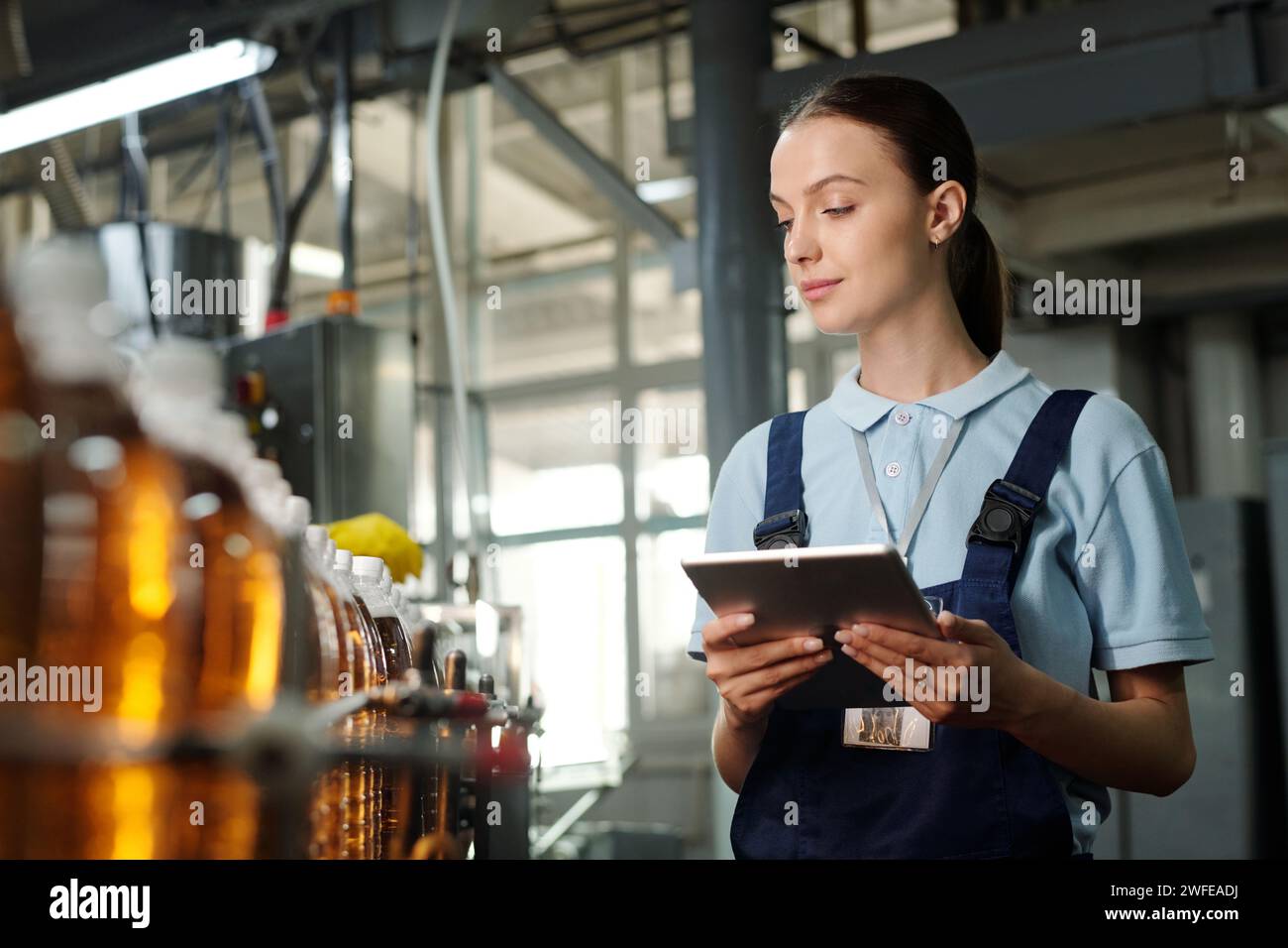 Young female inspector with tablet looking at assembly line with capped ...