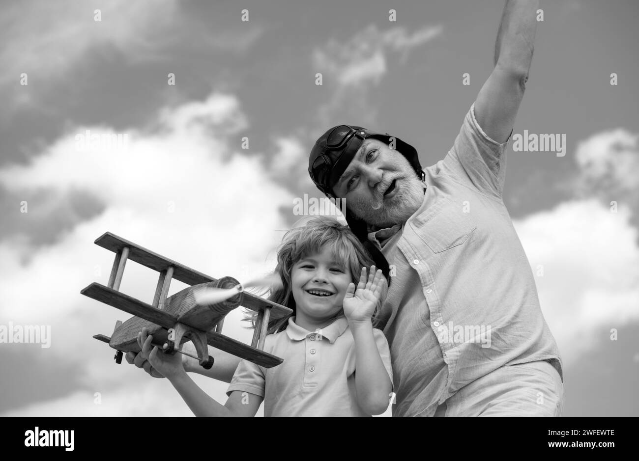 Funny grandfather and son playing with wooden plane against summer sky ...