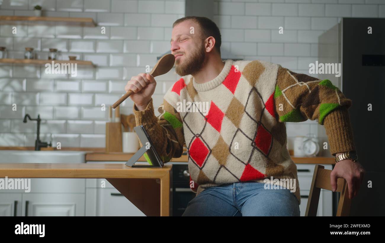 Cozy man singing into a ladle like a microphone while sit in the ...