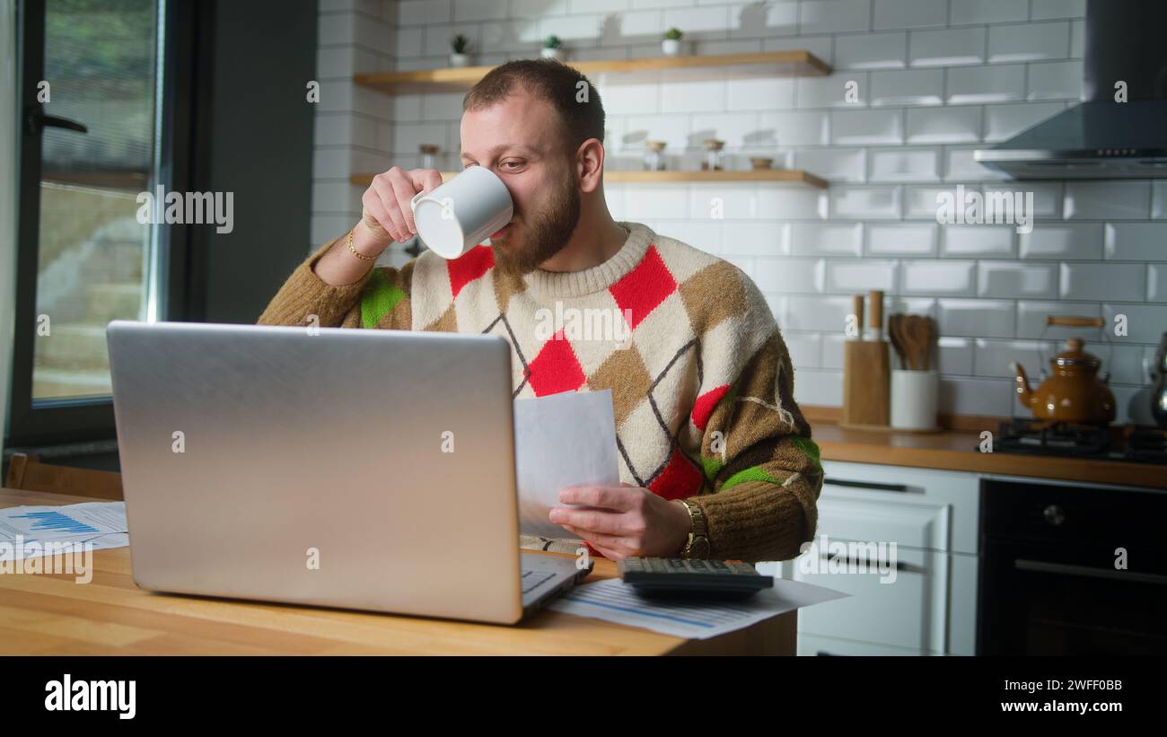 Adult man sitting in the kitchen with laptop pay bills, use calculator ...