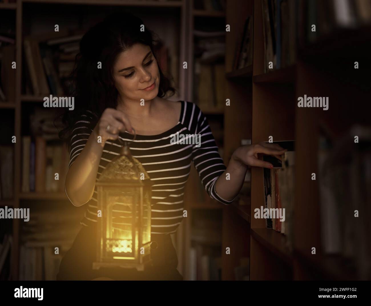 Attractive young librarian reading at night in the library, lit by a ...