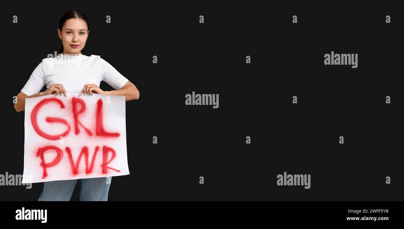 Young woman holding placard with slogan GRL PWR on dark background with ...