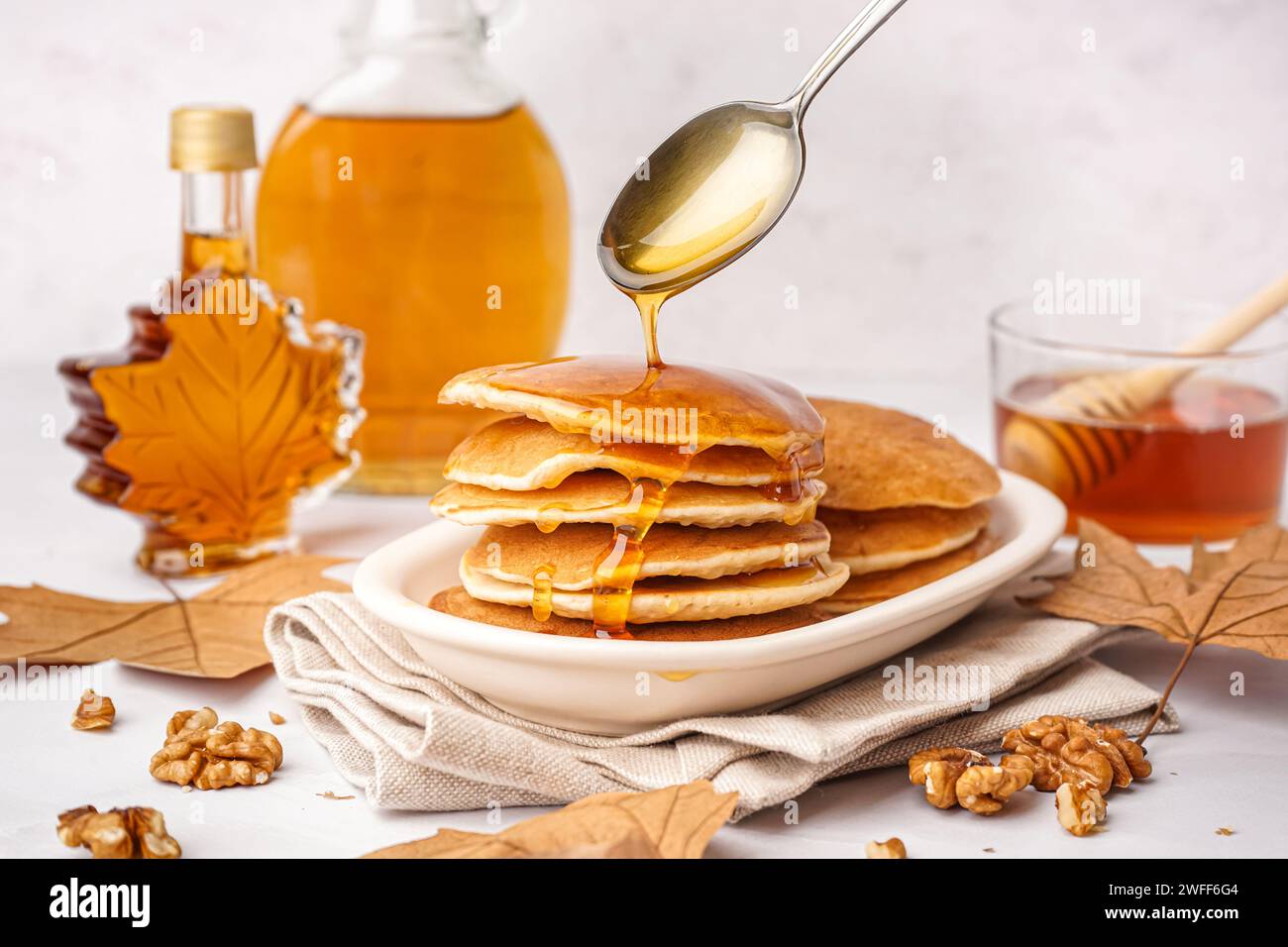 Pouring of maple syrup onto tasty pancakes on white background Stock ...