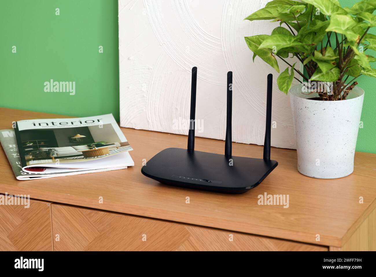 Modern wi-fi router with plant, magazines and painting on commode near ...