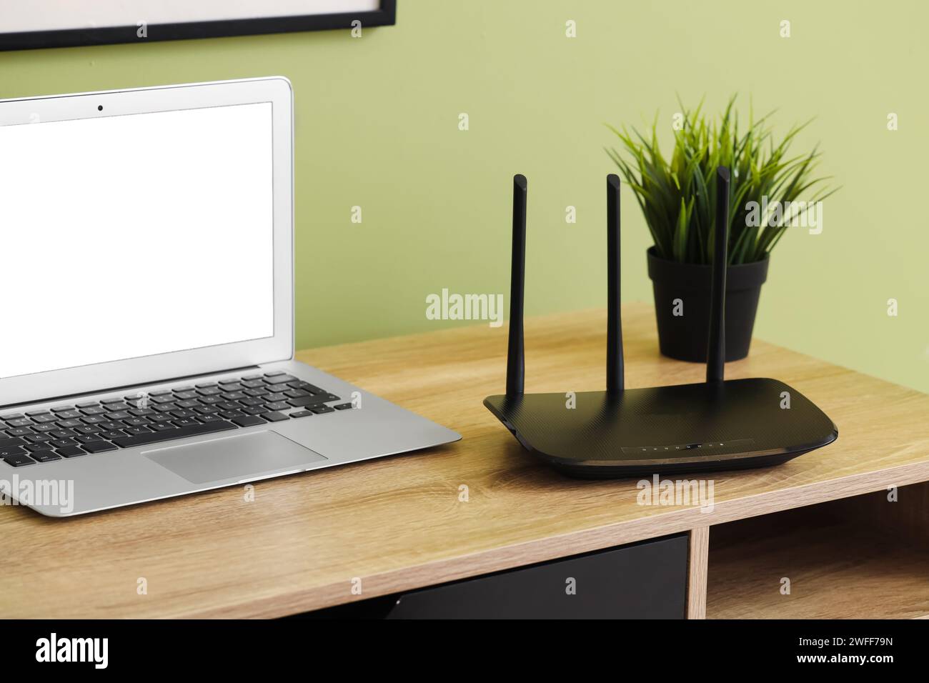 Modern wi-fi router with laptop on table near green wall in office ...