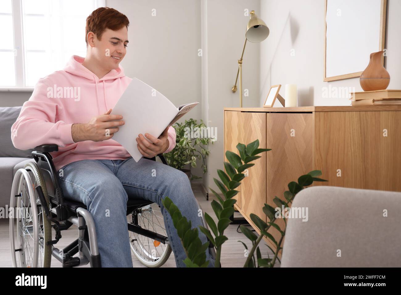 Young man in wheelchair reading magazine at home Stock Photo - Alamy