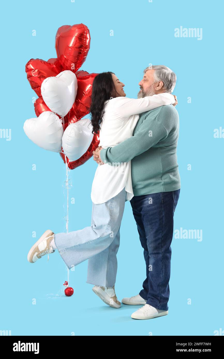 Beautiful mature couple with heart-shaped balloons hugging on blue ...