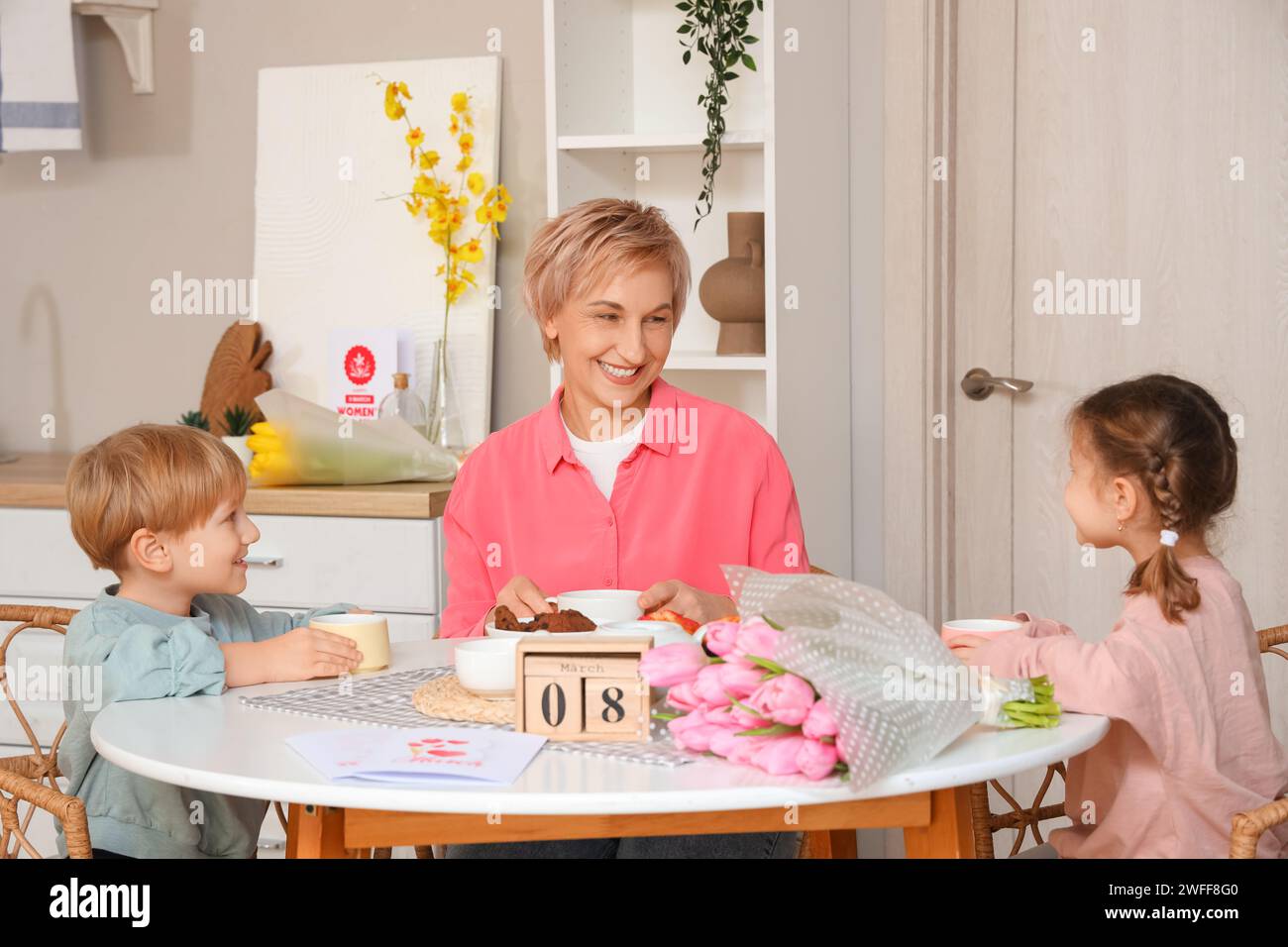Little children and their grandmother drinking tea at table in kitchen ...