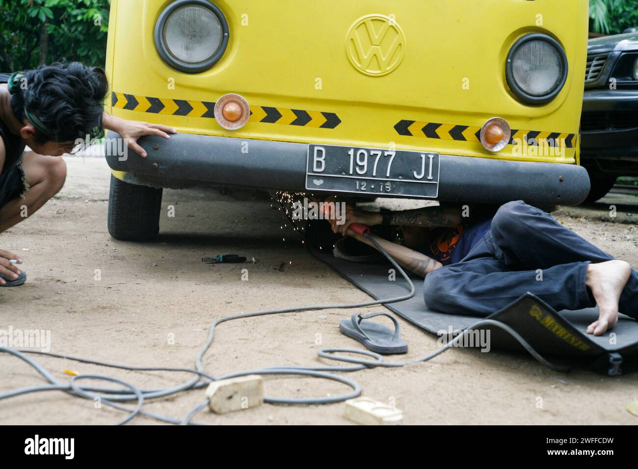 a young man fixing a steering problem on an old car, under the car ...