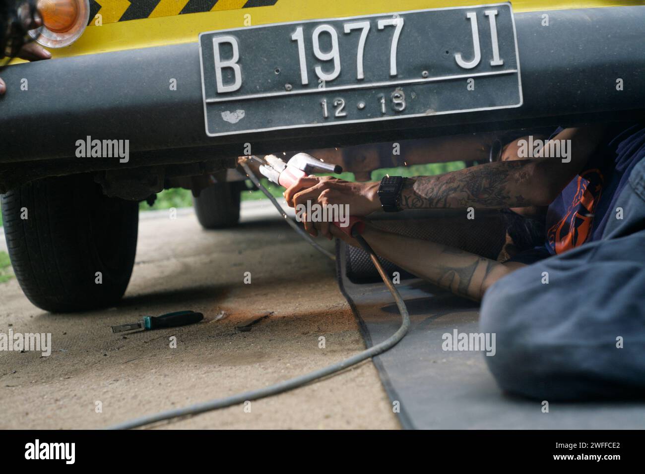 a young man fixing a steering problem on an old car, under the car ...
