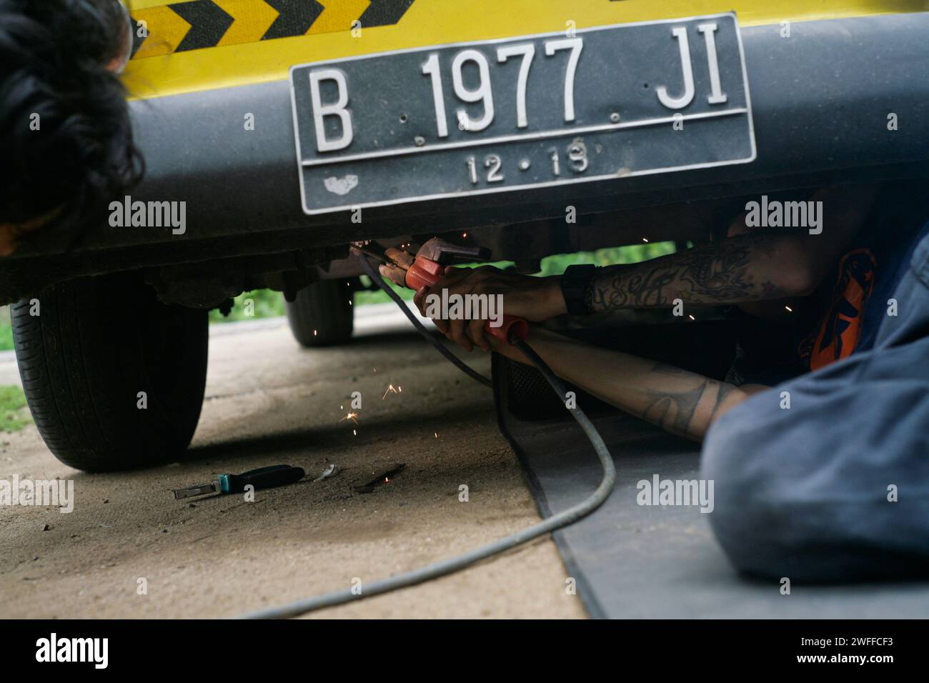 a young man fixing a steering problem on an old car, under the car ...