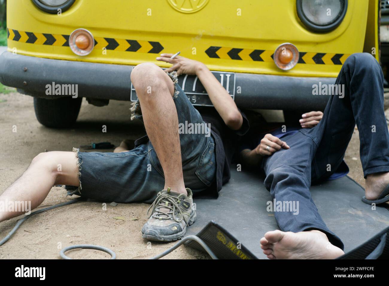 a young man fixing a steering problem on an old car, under the car ...