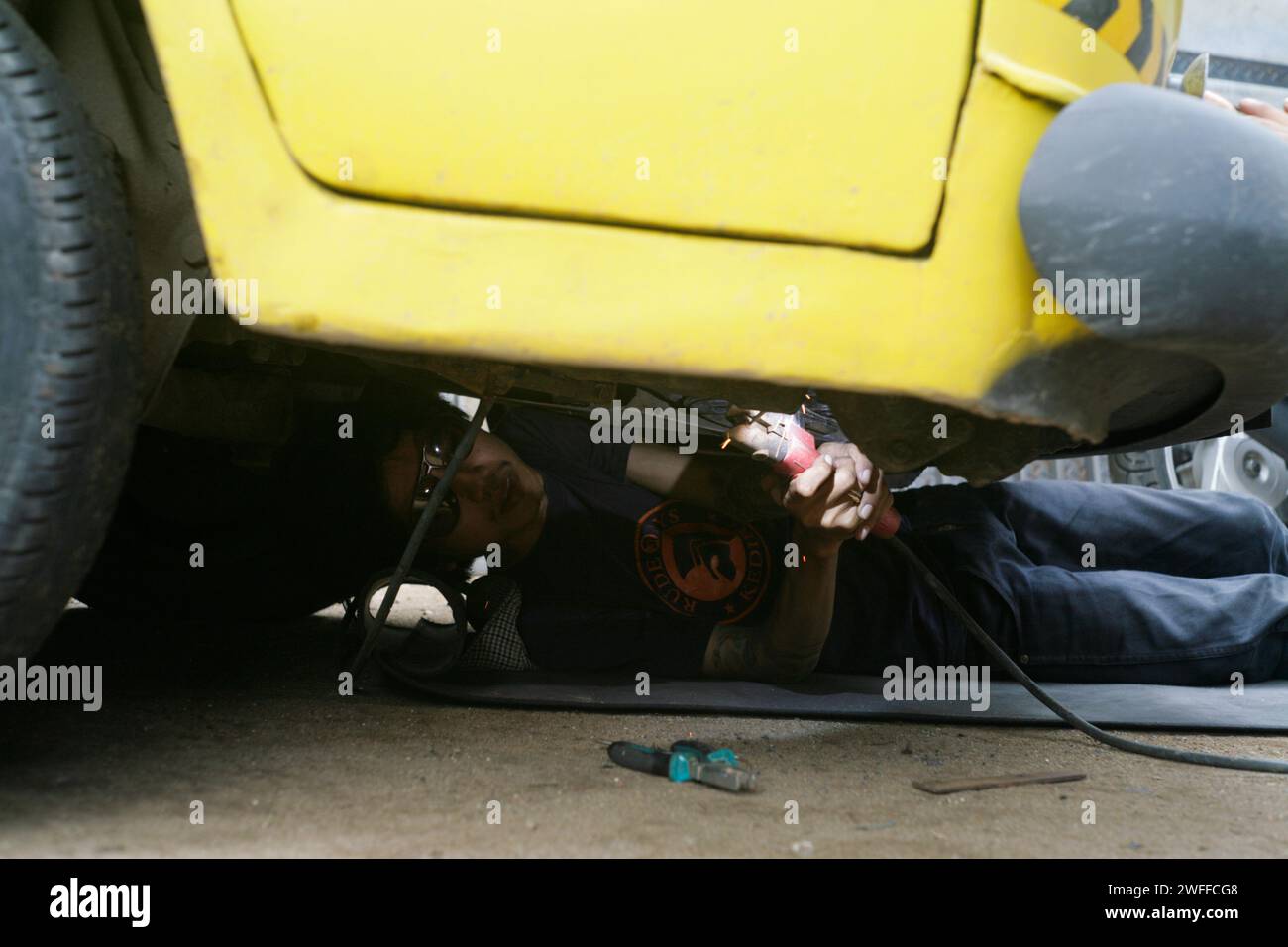 a young man fixing a steering problem on an old car, under the car ...