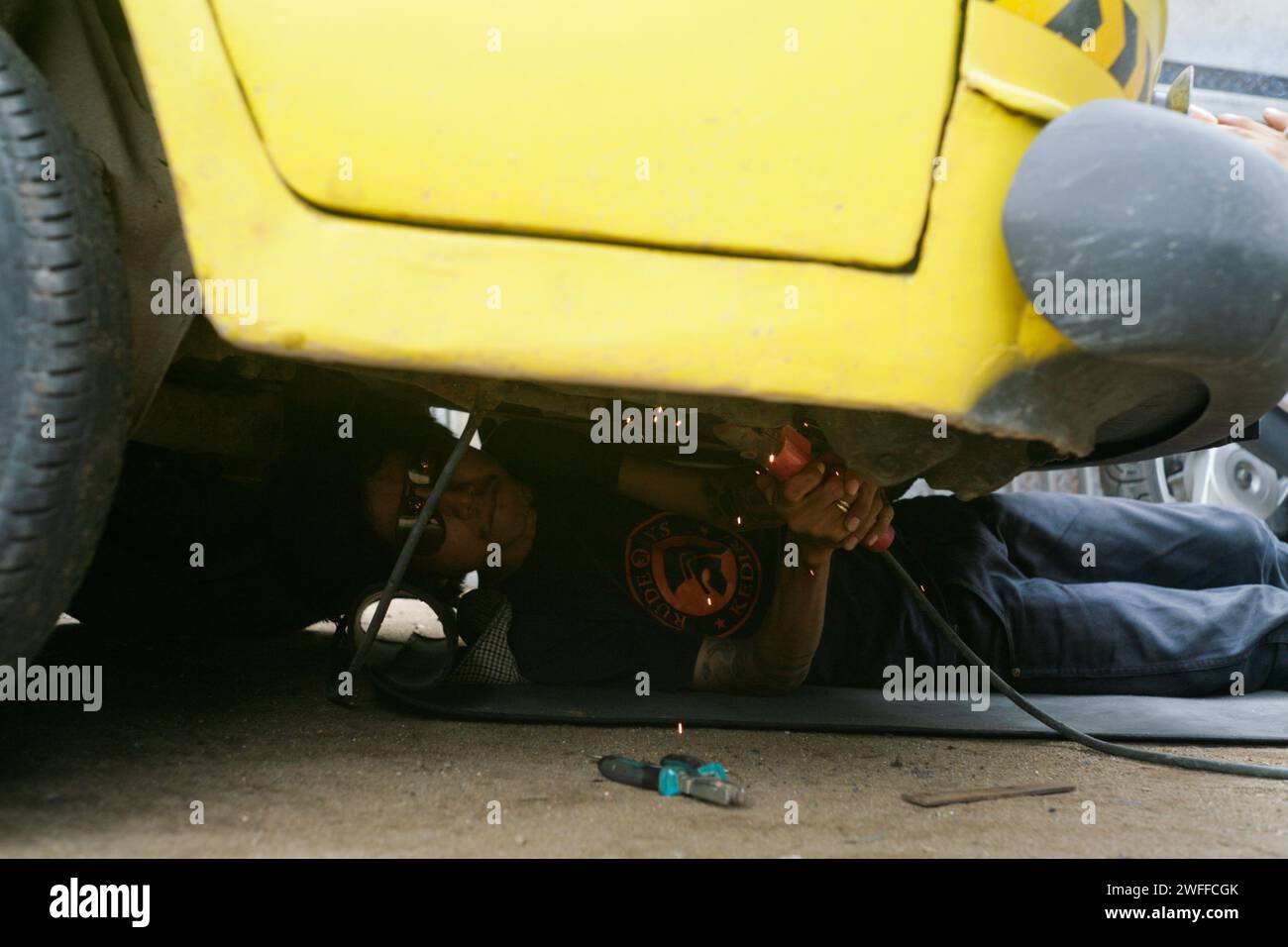 a young man fixing a steering problem on an old car, under the car ...
