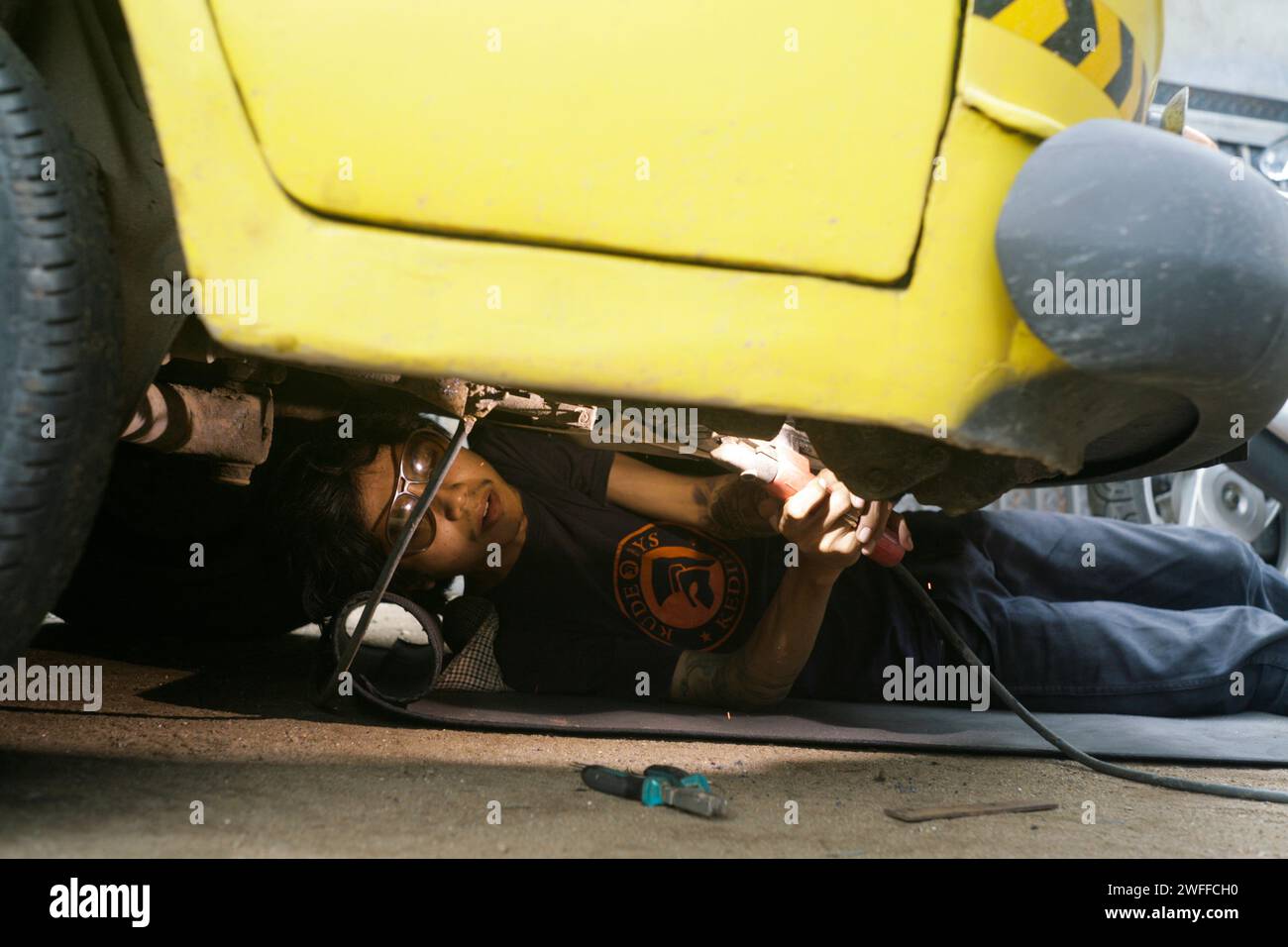 a young man fixing a steering problem on an old car, under the car ...