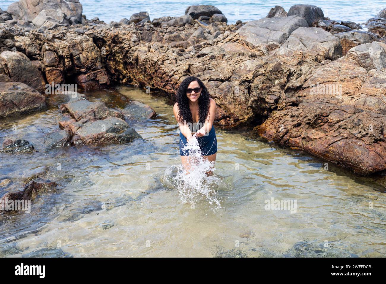 Beautiful woman in a puddle on the beach, throwing water into the air ...