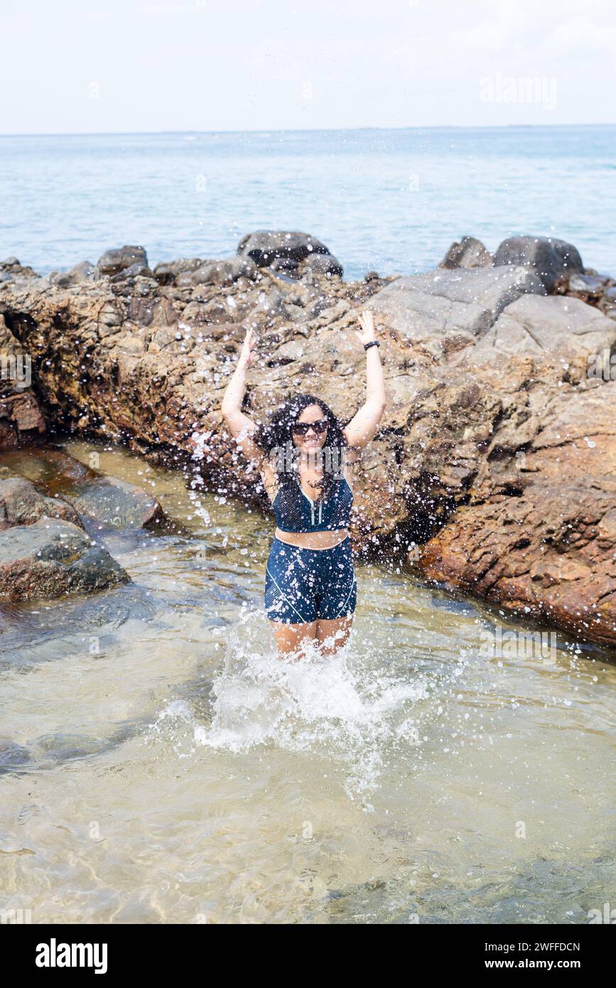 Beautiful woman in a puddle on the beach, throwing water into the air ...