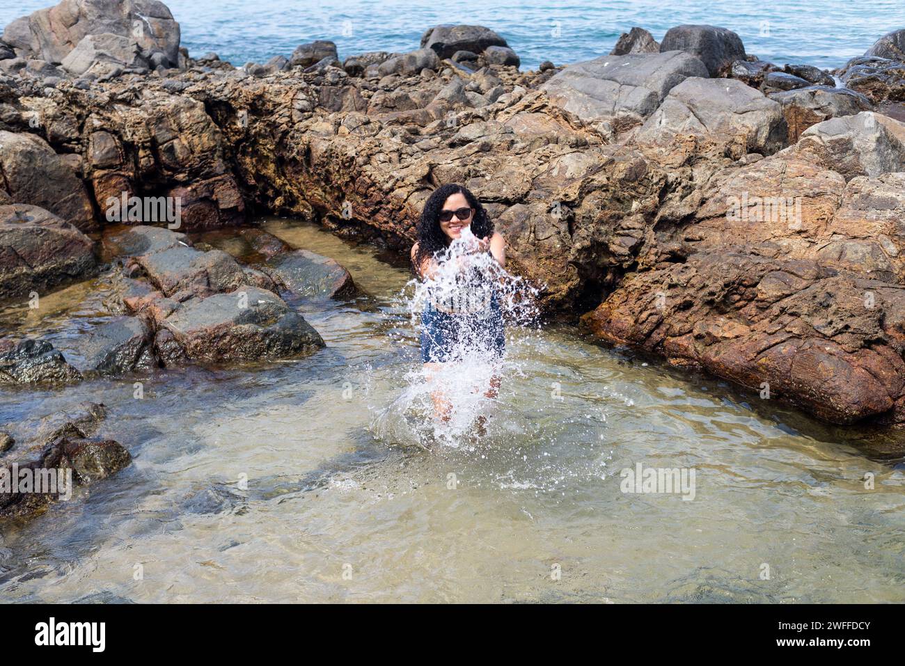 Beautiful woman in a puddle on the beach, throwing water into the air ...