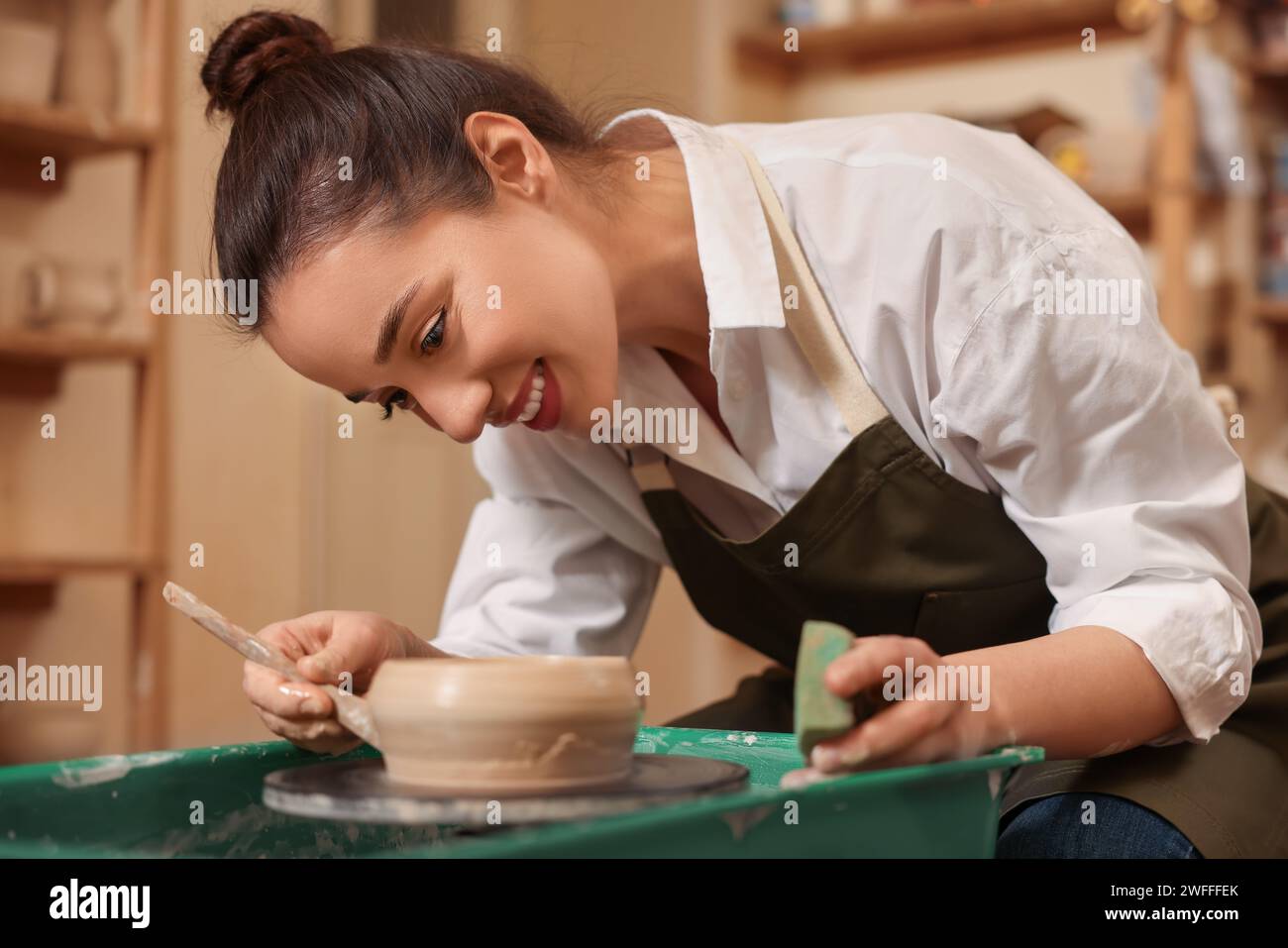 Clay crafting. Smiling woman making bowl with modeling tool on potter's ...