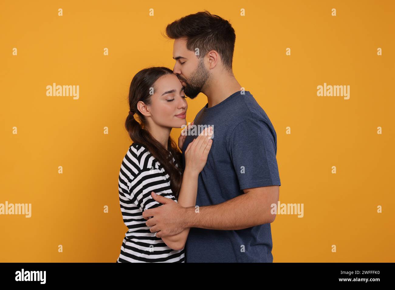 Man kissing his girlfriend on orange background Stock Photo - Alamy
