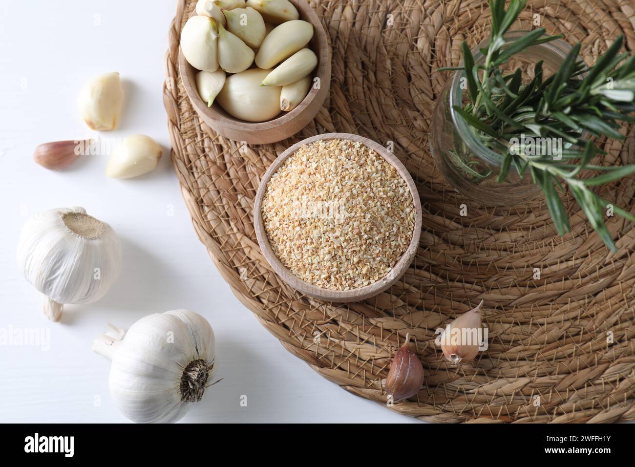 Dehydrated garlic granules in bowl, rosemary and fresh cloves on white ...