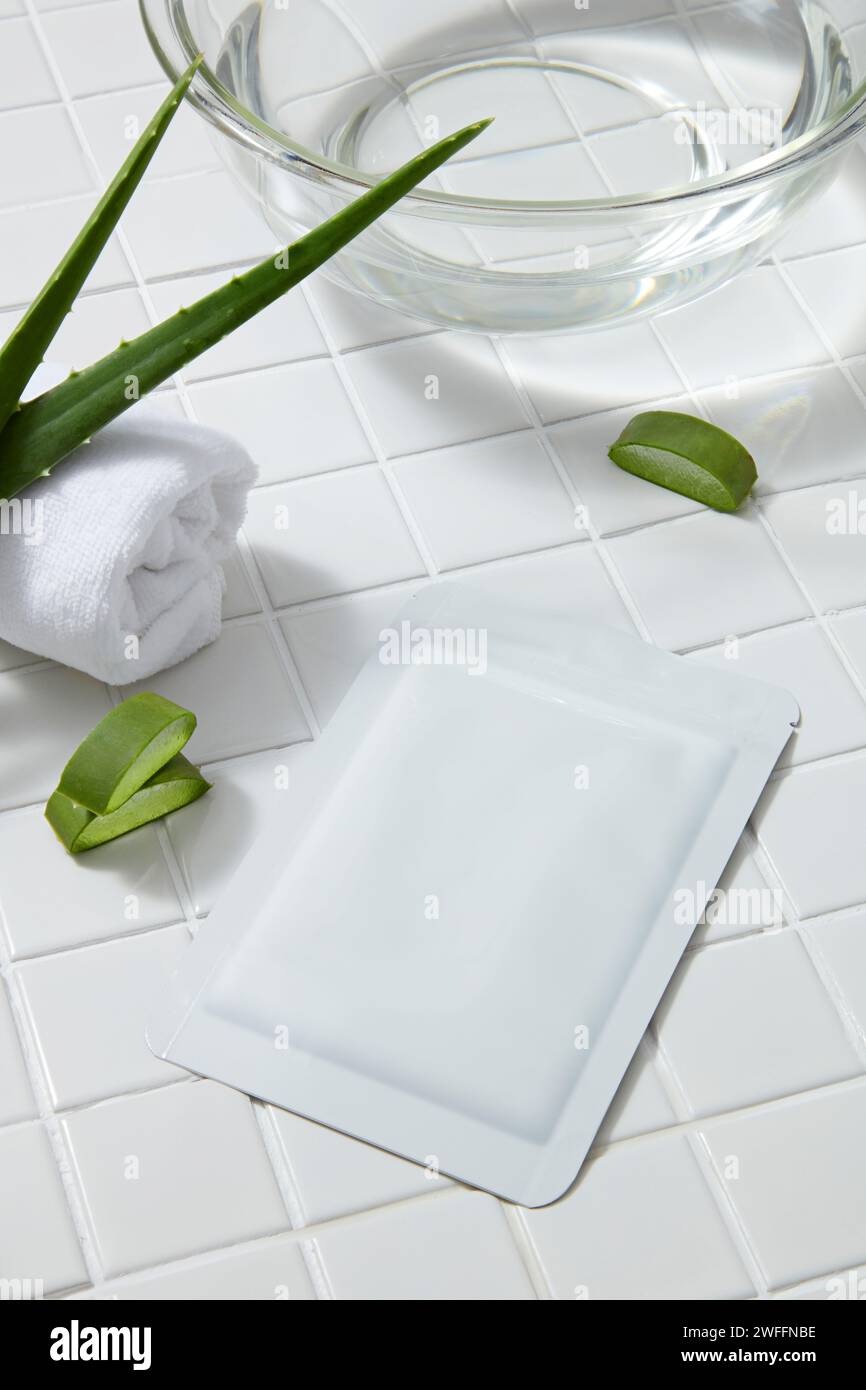 A mask sheet placed on white tile background with fresh Aloe vera ...