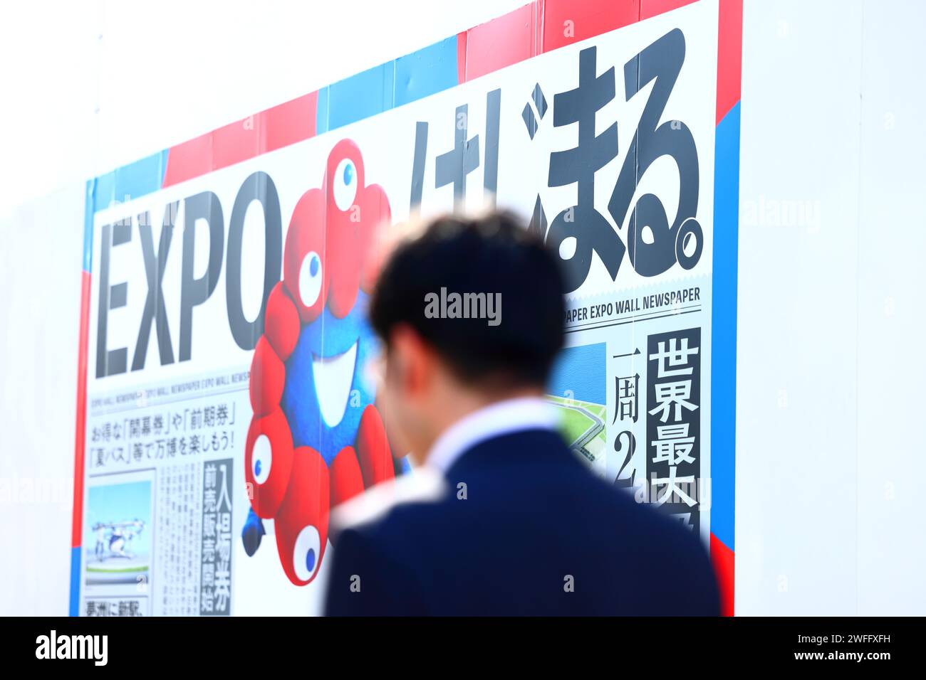 A Pedestrian walks past EXPO WALL NEWSPAPER for the 2025 World Expo is ...