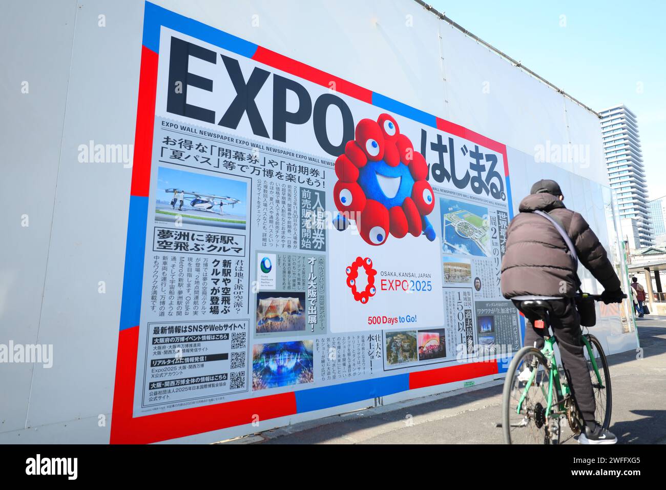 Pedestrians walk past EXPO WALL NEWSPAPER for the 2025 World Expo is ...