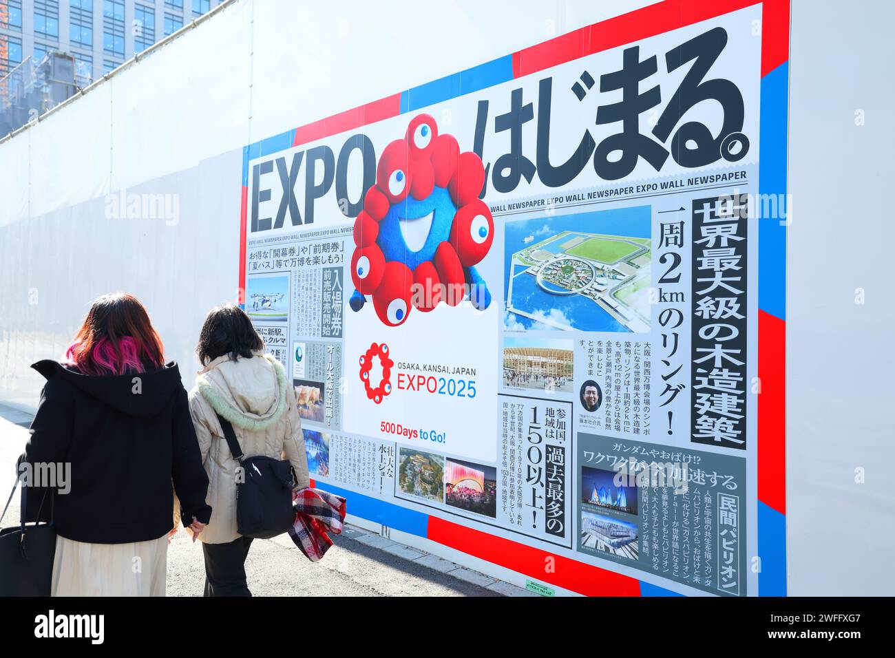 Pedestrians walk past EXPO WALL NEWSPAPER for the 2025 World Expo is ...