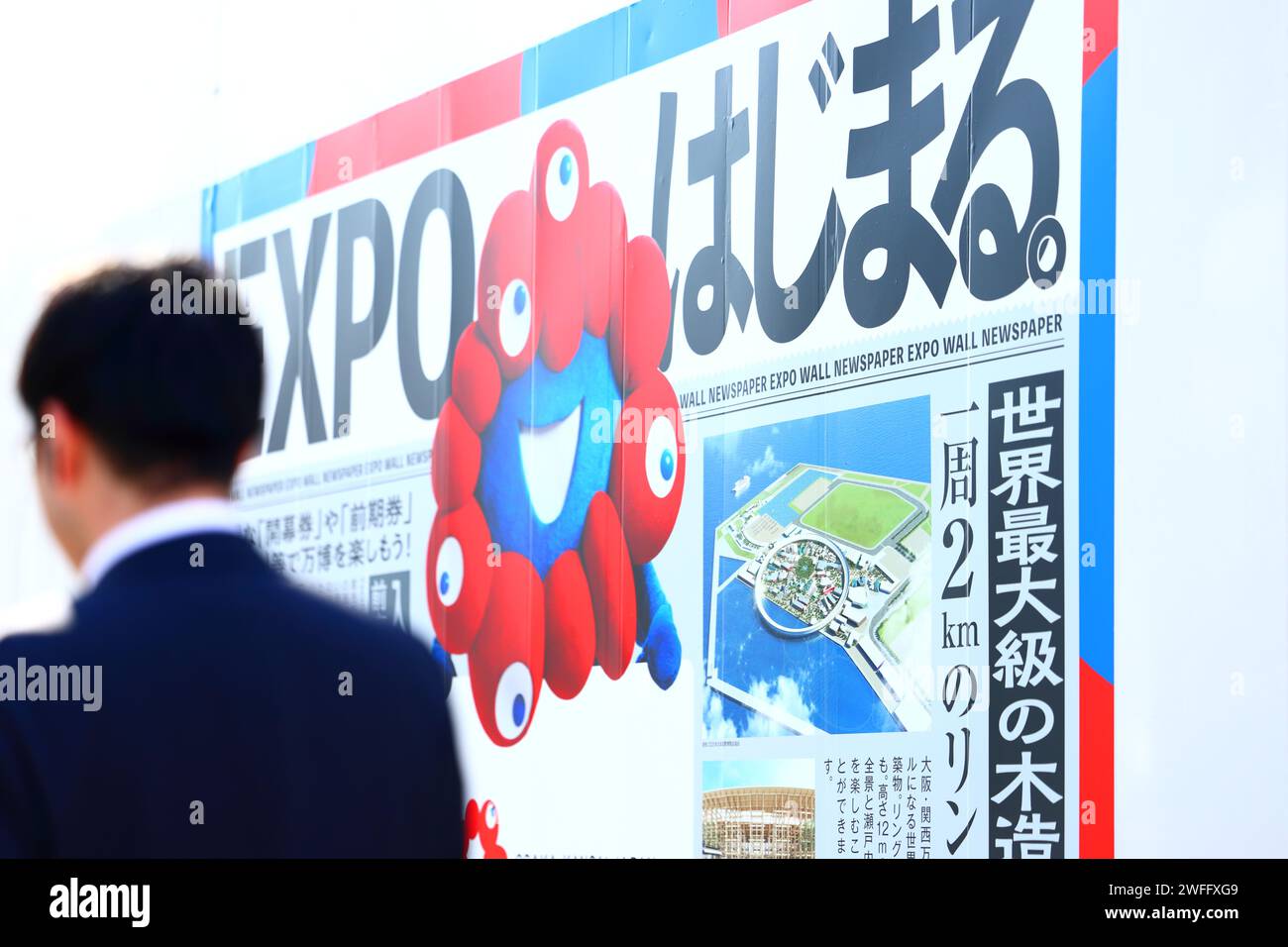 A Pedestrian walks past EXPO WALL NEWSPAPER for the 2025 World Expo is ...