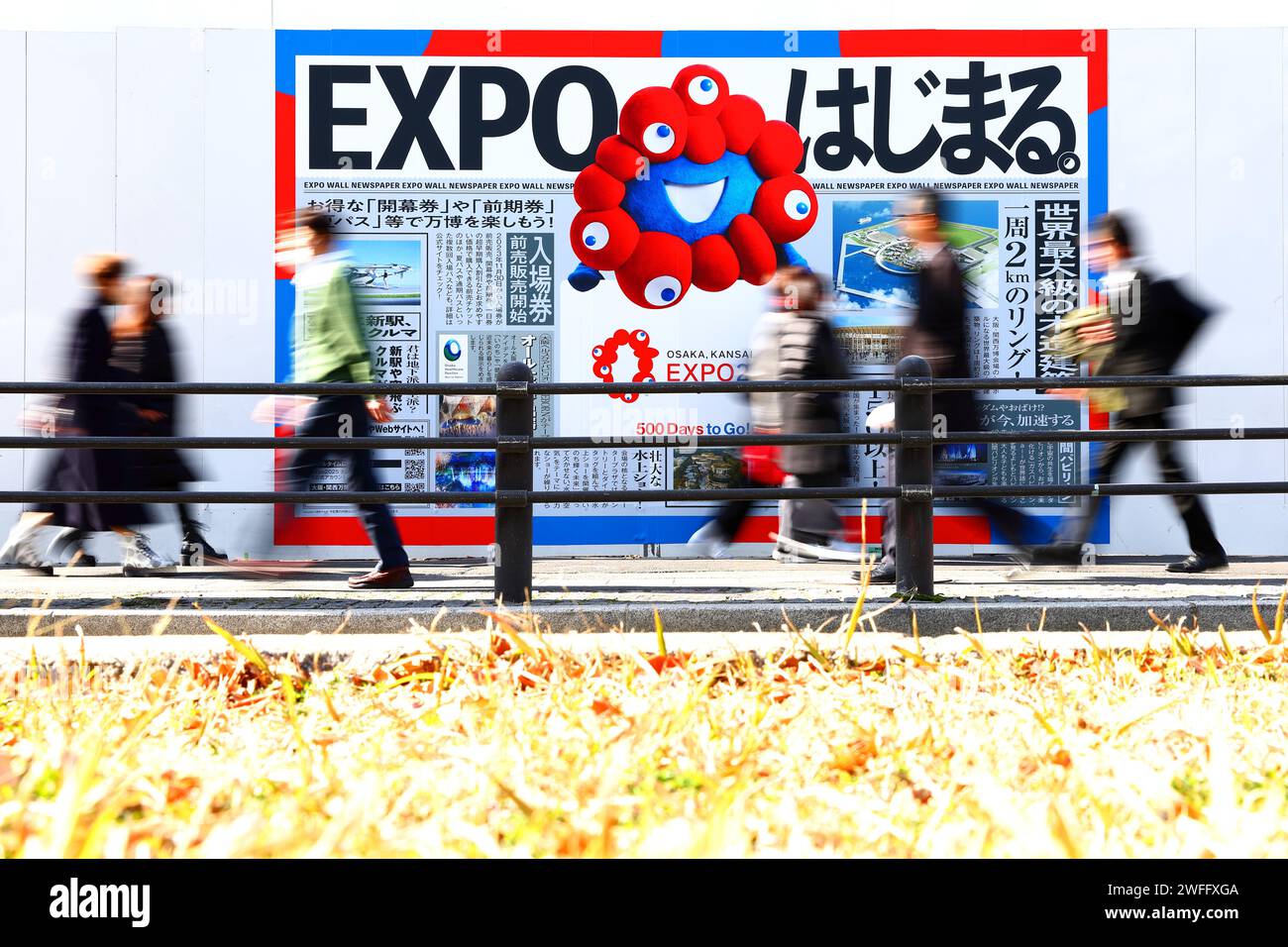 Pedestrians walk past EXPO WALL NEWSPAPER for the 2025 World Expo is ...