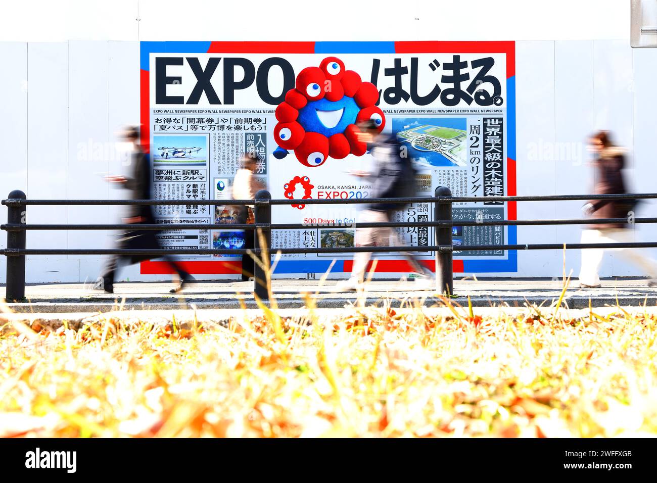 Pedestrians walk past EXPO WALL NEWSPAPER for the 2025 World Expo is ...