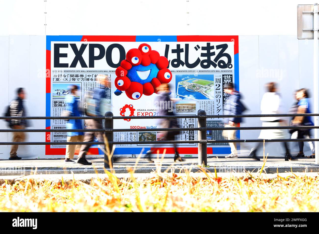 Pedestrians walk past EXPO WALL NEWSPAPER for the 2025 World Expo is ...