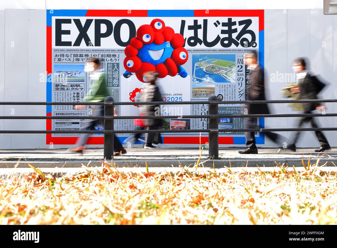 Pedestrians walk past EXPO WALL NEWSPAPER for the 2025 World Expo is ...