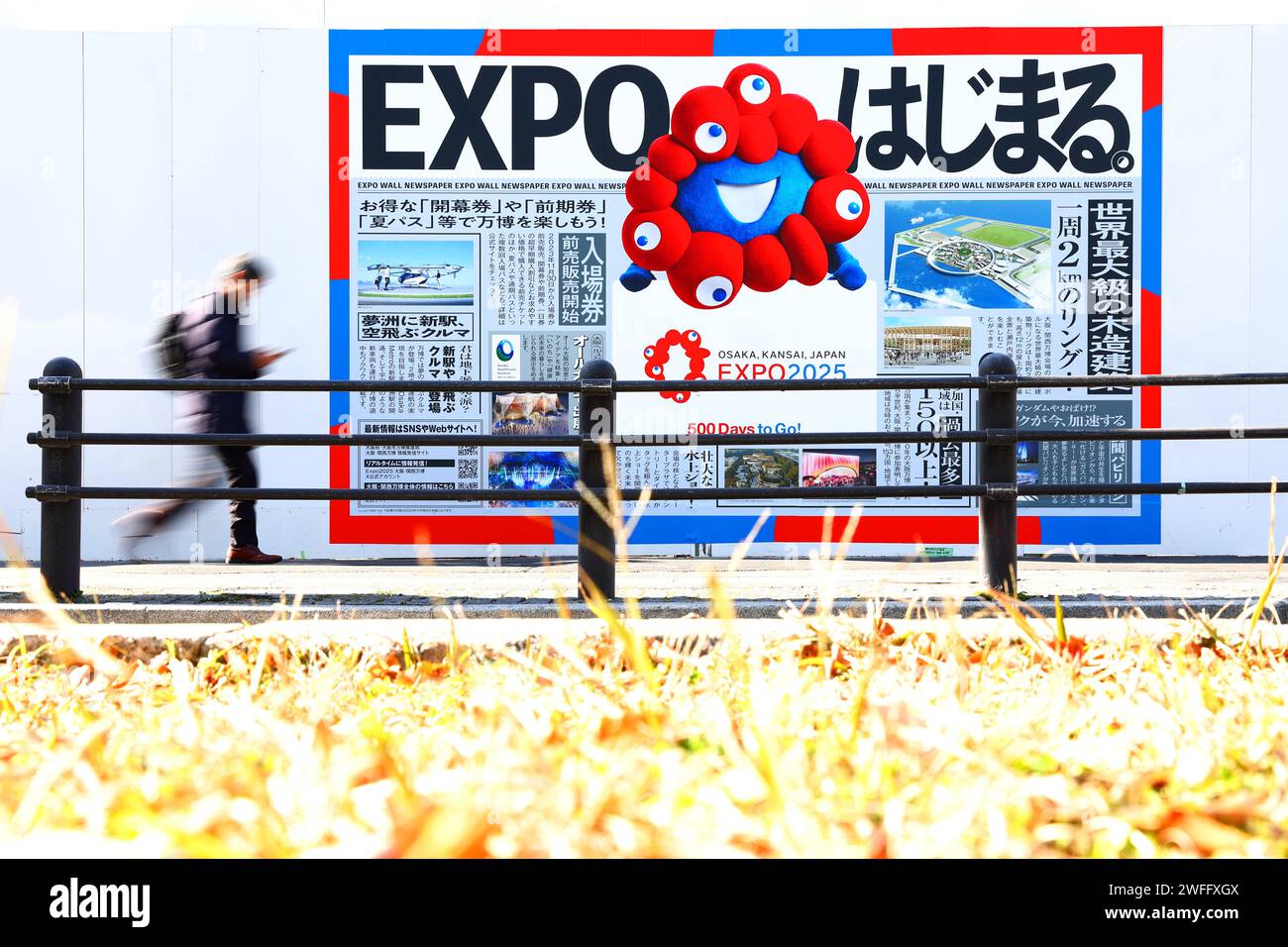Pedestrians walk past EXPO WALL NEWSPAPER for the 2025 World Expo is ...