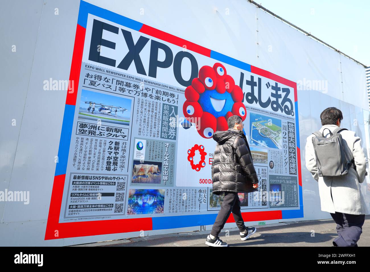 Pedestrians walk past EXPO WALL NEWSPAPER for the 2025 World Expo is ...