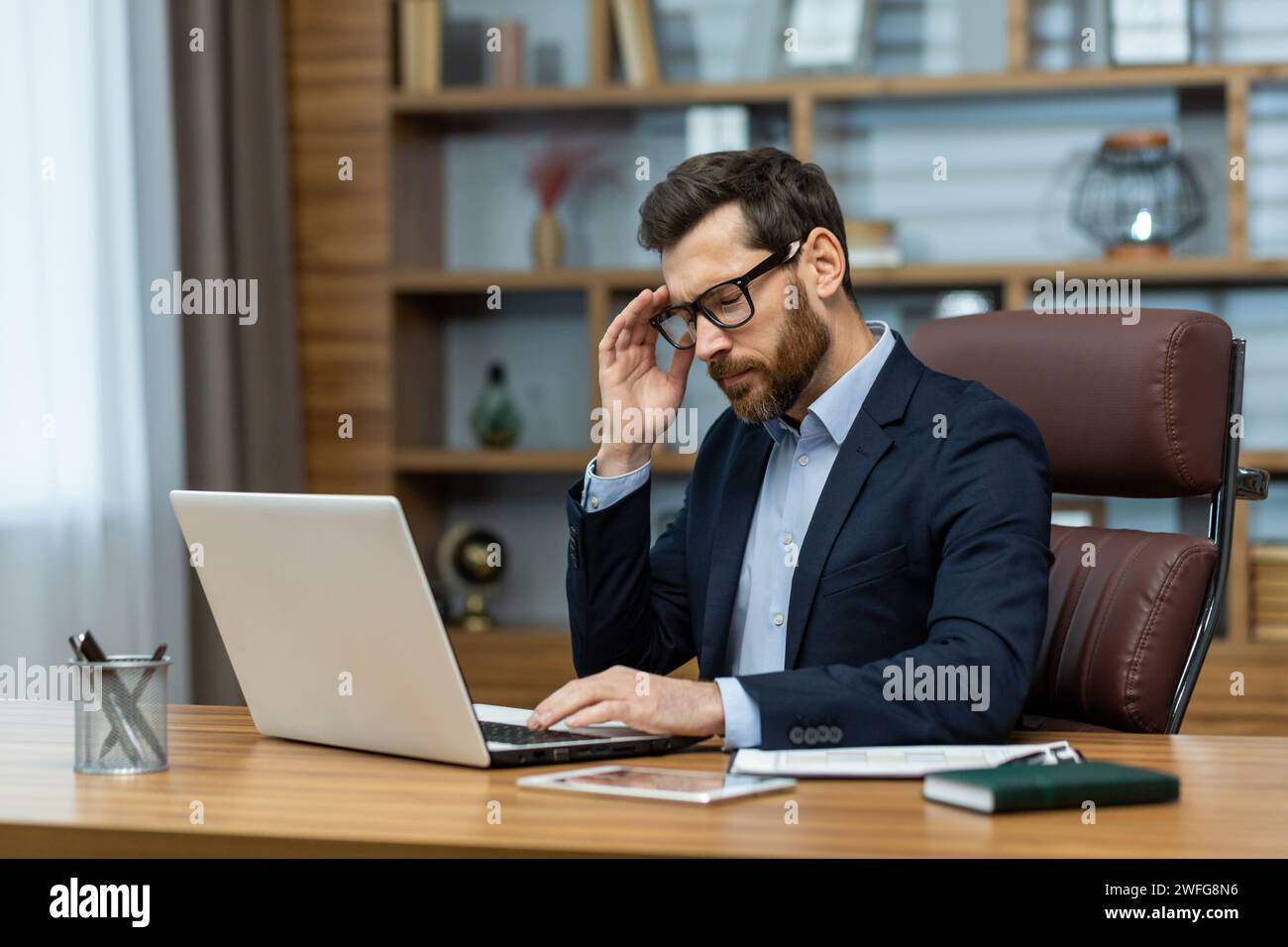 Frustrated administrator experiencing headache while sitting by desk ...