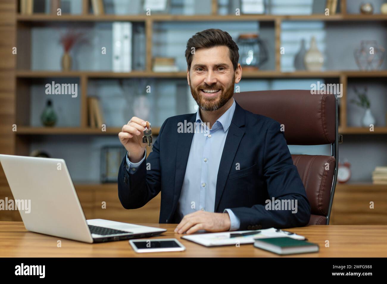 Happy attractive man in shirt and jacket sitting by desktop with laptop ...