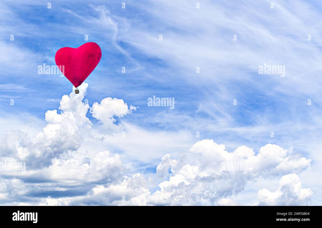 Red heart-shaped hot air balloon flying over a blue sky with white ...