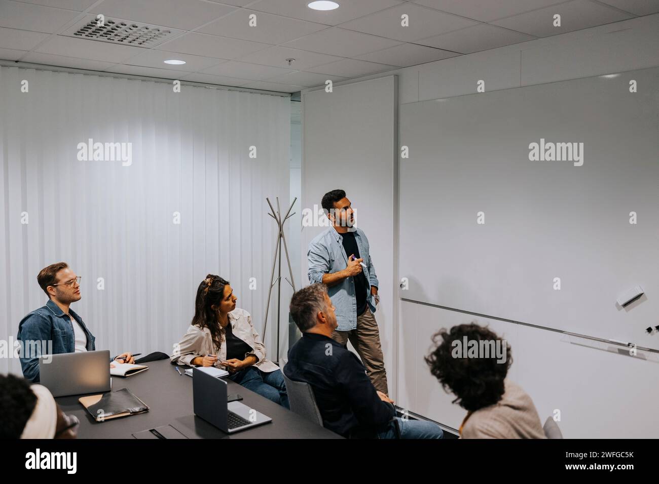 Mature businessman explaining strategy on whiteboard to colleagues in ...