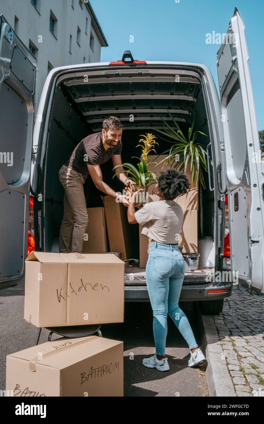 Multiracial couple helping each other while unloading plants from van ...