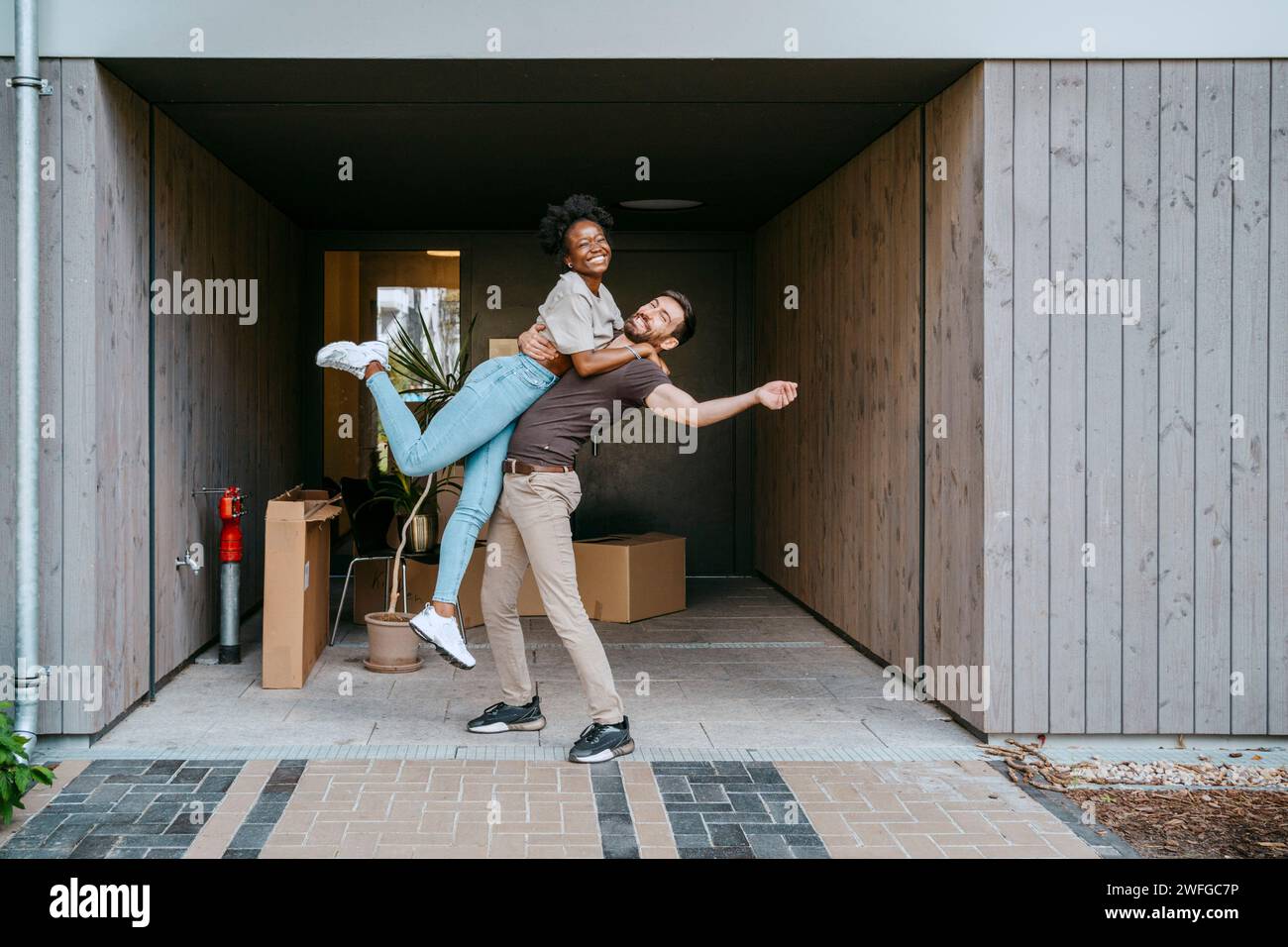 Happy man picking up girlfriend while standing at building entrance ...