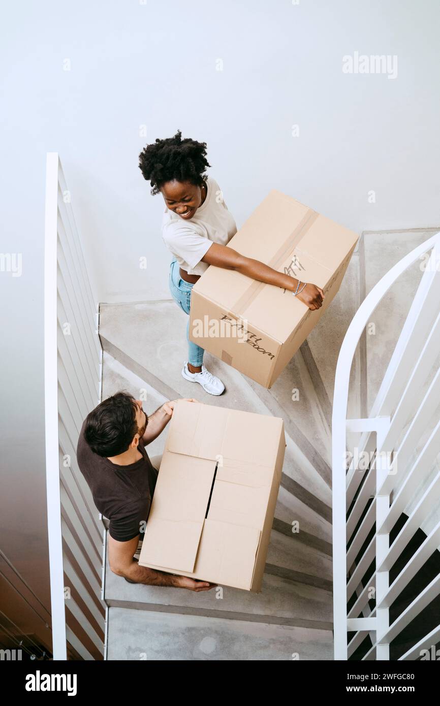 High angle view of multiracial couple carrying boxes while moving up on ...