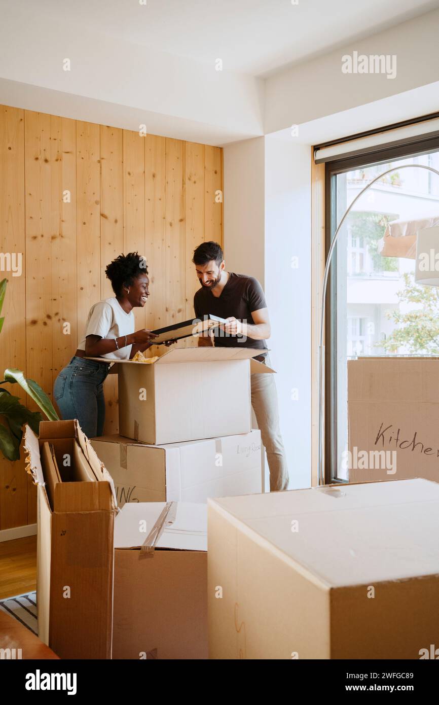 Multiracial couple removing frame from cardboard box while standing at ...