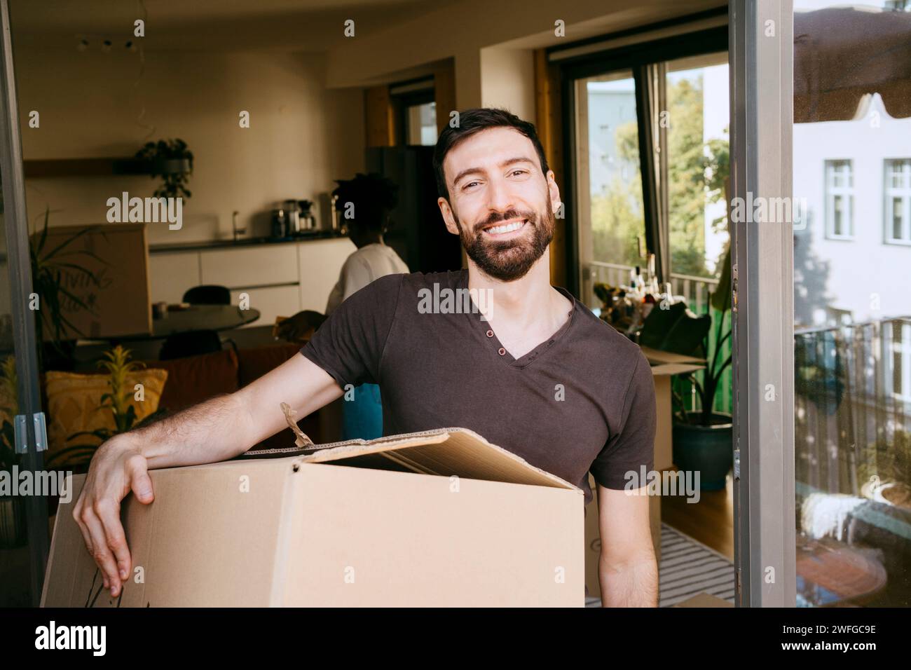 Portrait of smiling man carrying cardboard box at new home Stock Photo ...
